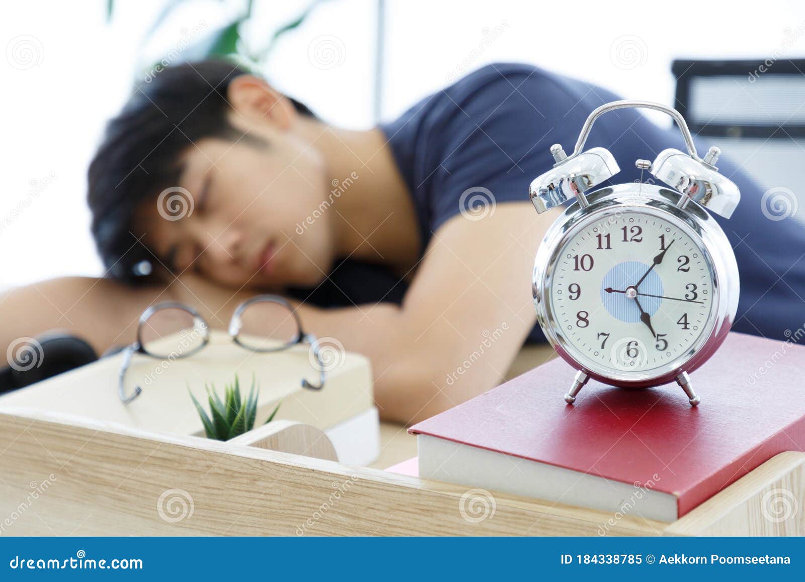 Clock on Table in Front of Tired Asian Man Napping at a Office after a ...