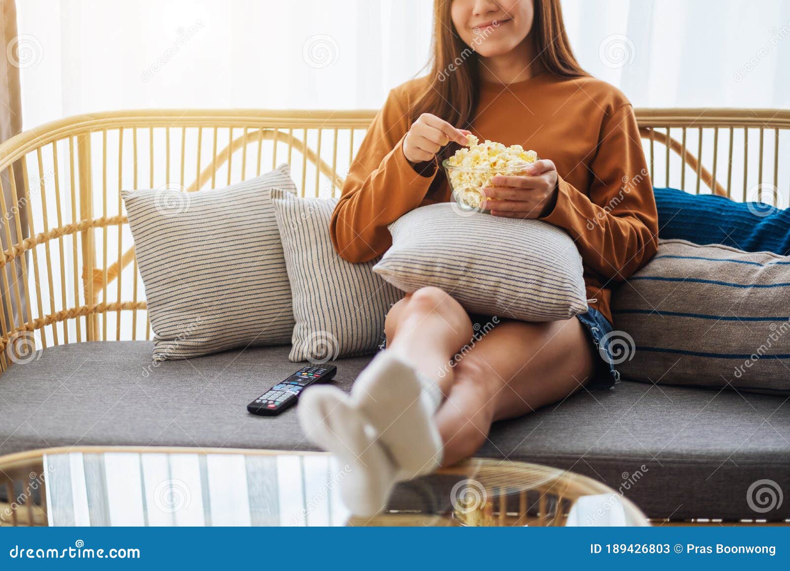 A Young Woman Holding And Eating Pop Corn While Watching Tv And Sitting