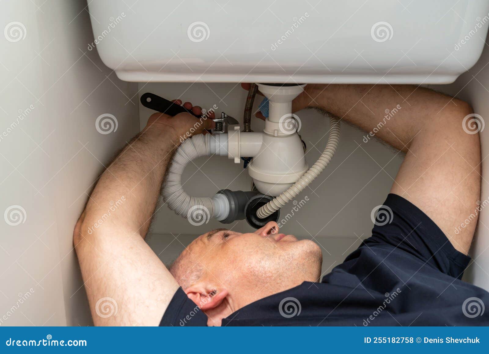 Close-up of a Man in a Difficult Position Trying To Fix the Pipe Under ...