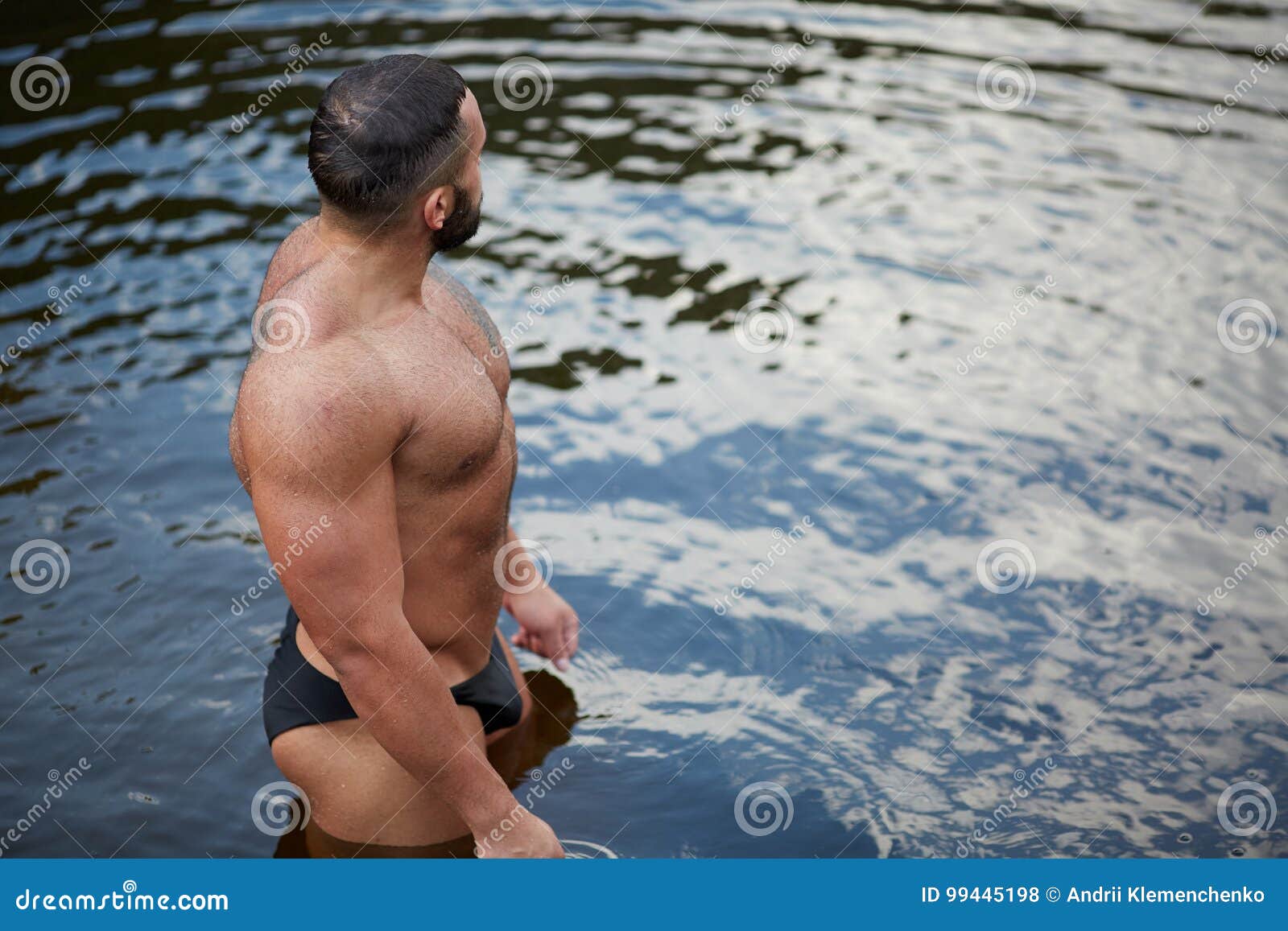 A Muscular Man In Swimming Trunks Looking Into The Distance On The Sea