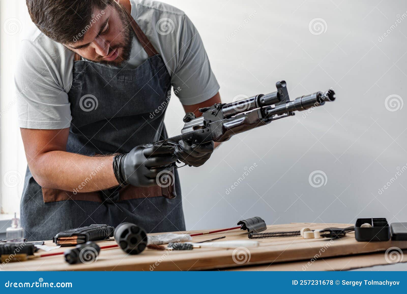 Close Up of Young Man in Apron Disassembling a Gun Above the Table ...