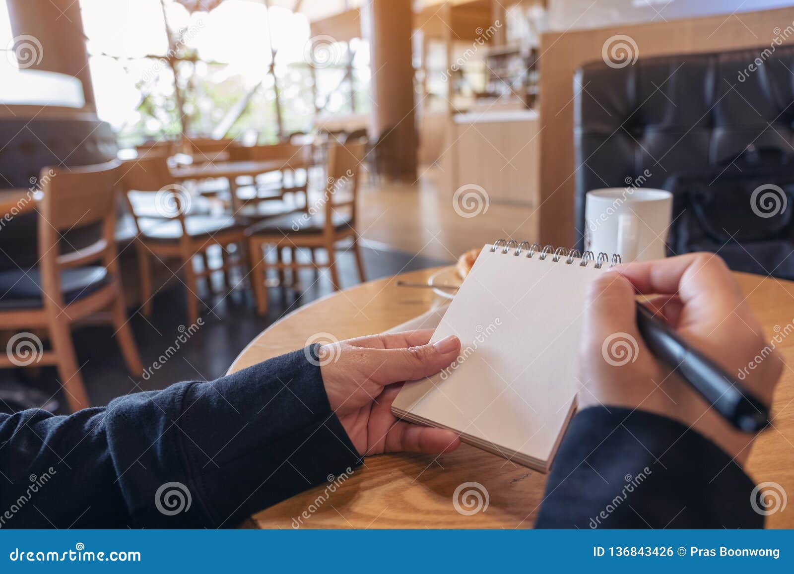 A Hand Holding and Writing on Blank Notebook on Table in Cafe Stock ...
