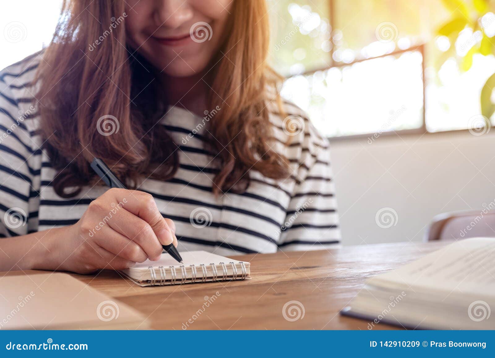 A Woman Writing on Blank Notebook and Books on Wooden Table while ...