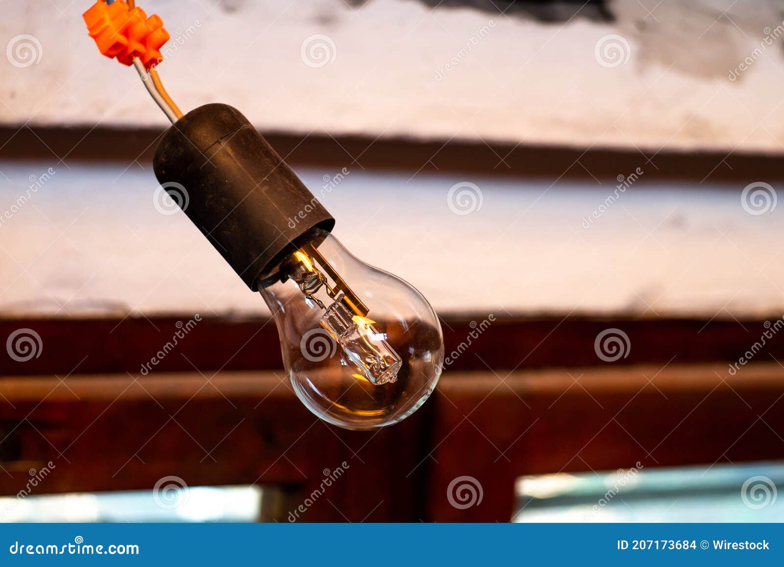 Closeup of a Light Bulb Hanging from Wires on a Wall with a Blurry ...