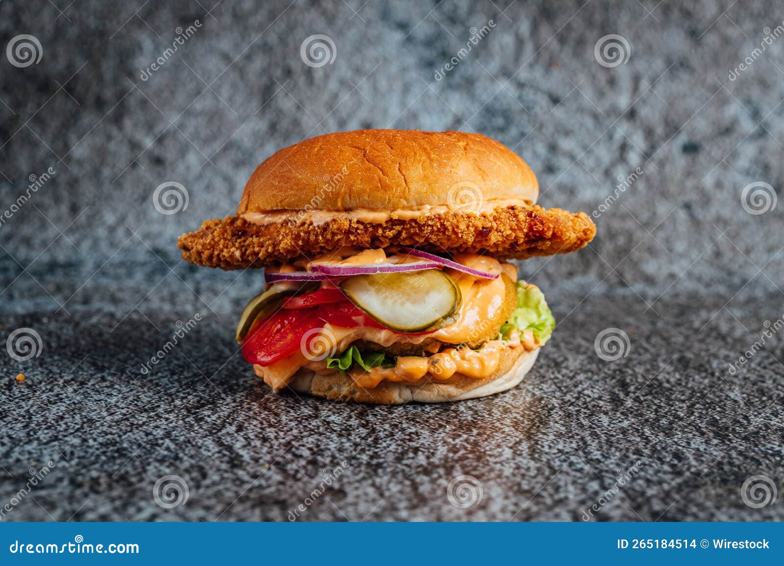 Closeup Shot of a Large Fried Chicken Cheeseburger with Vegetables on a ...
