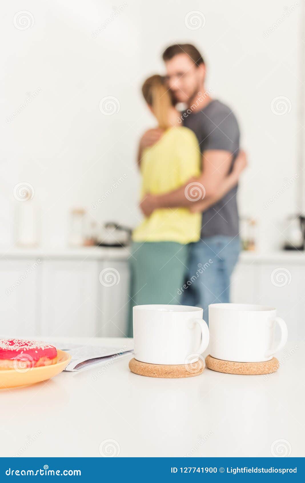 Closeup Shot of Two Coffee Cups at Table with Donuts and Couple Hugging ...