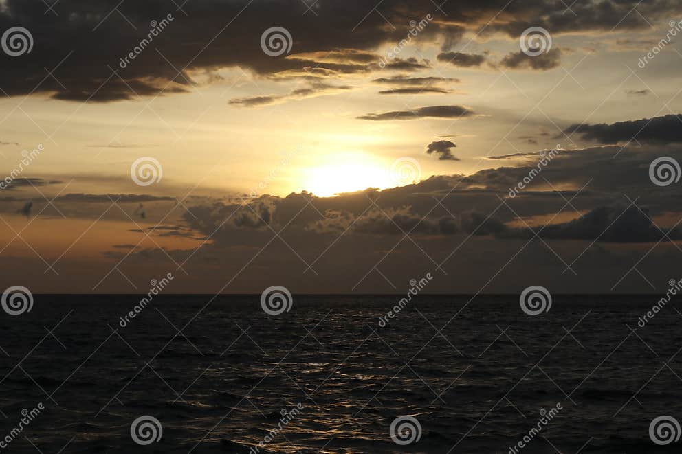 A Cloudy Sky Over the Ocean with a Dark Sky and the Sun Setting Behind ...