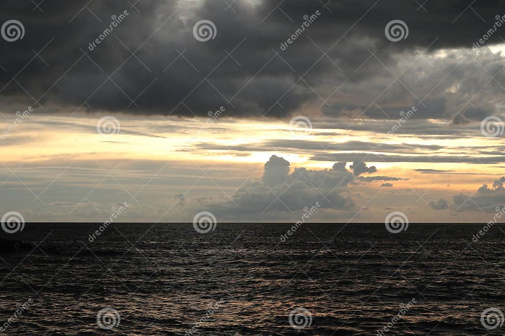 A Cloudy Sky Over the Ocean with a Dark Sky and the Sun Setting Behind ...