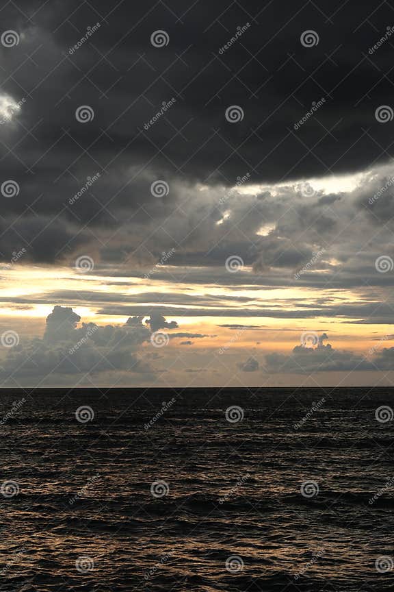 A Cloudy Sky Over the Ocean with a Dark Sky and the Sun Setting Behind ...