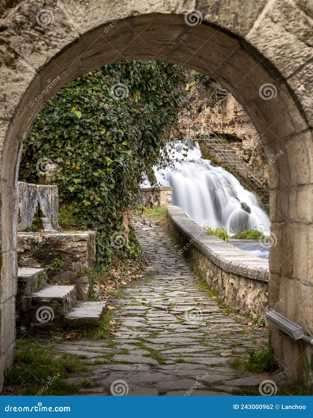 A Cobbled Path through an Arch with a Waterfall in the Background Stock ...