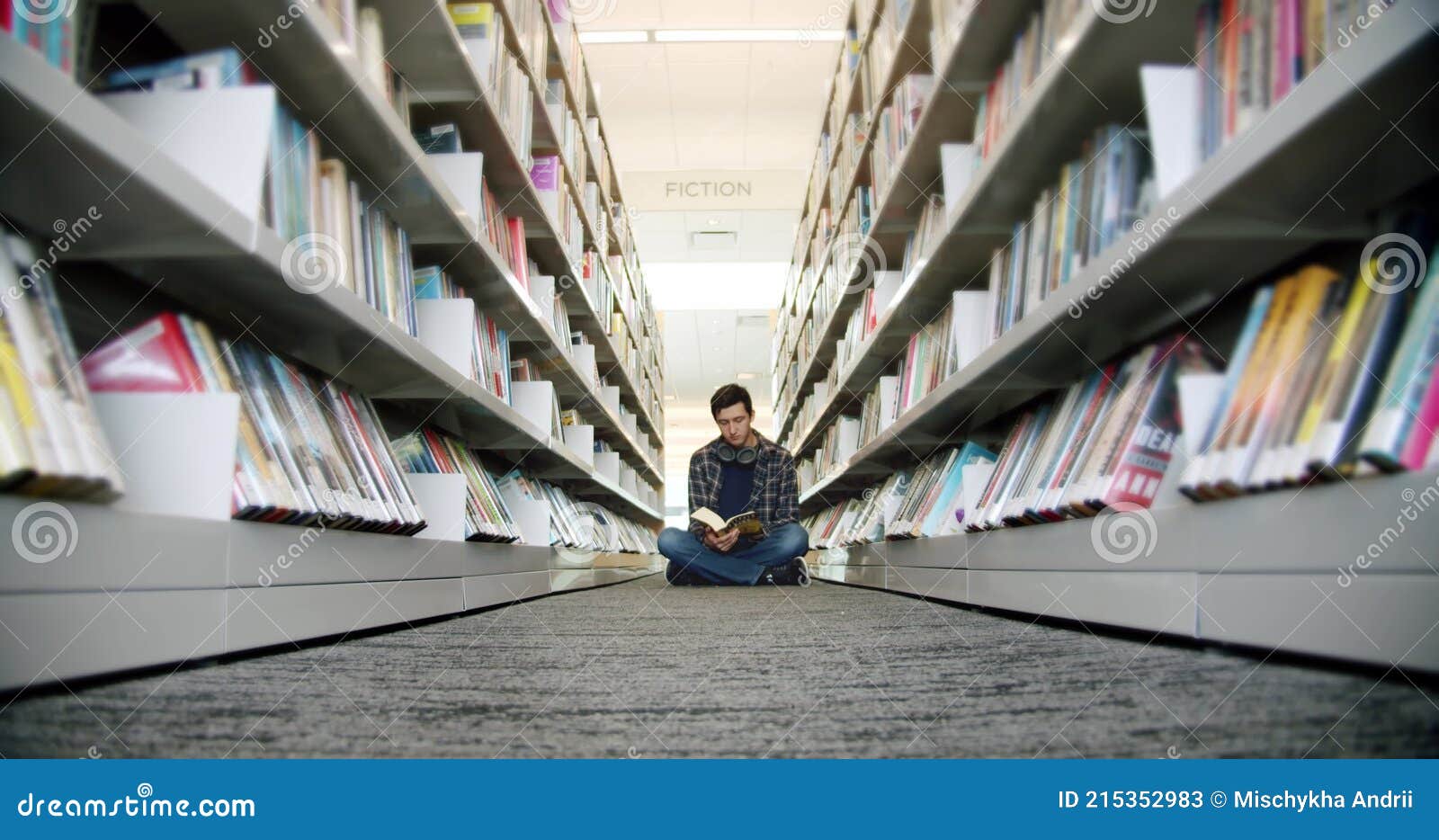 College Student Sitting on the Floor in the Library and Reading a Book ...