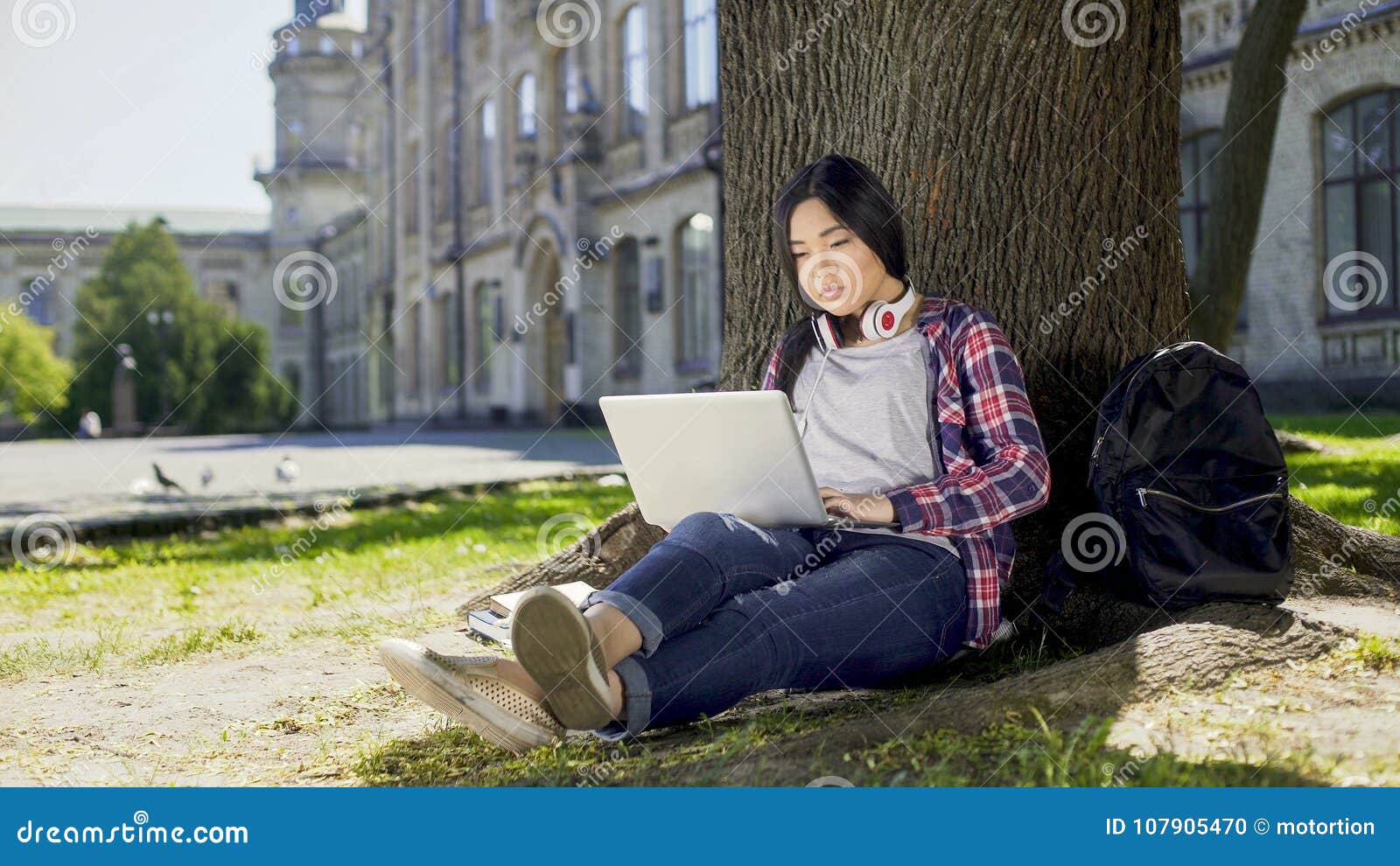 College Student Sitting Under Tree in Campus, Using Laptop, Writing ...