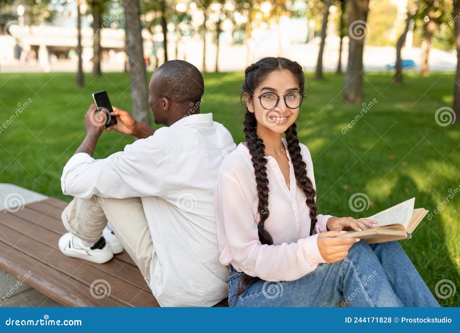 College Students Sitting Back To Back, Using Smartphone and Book ...