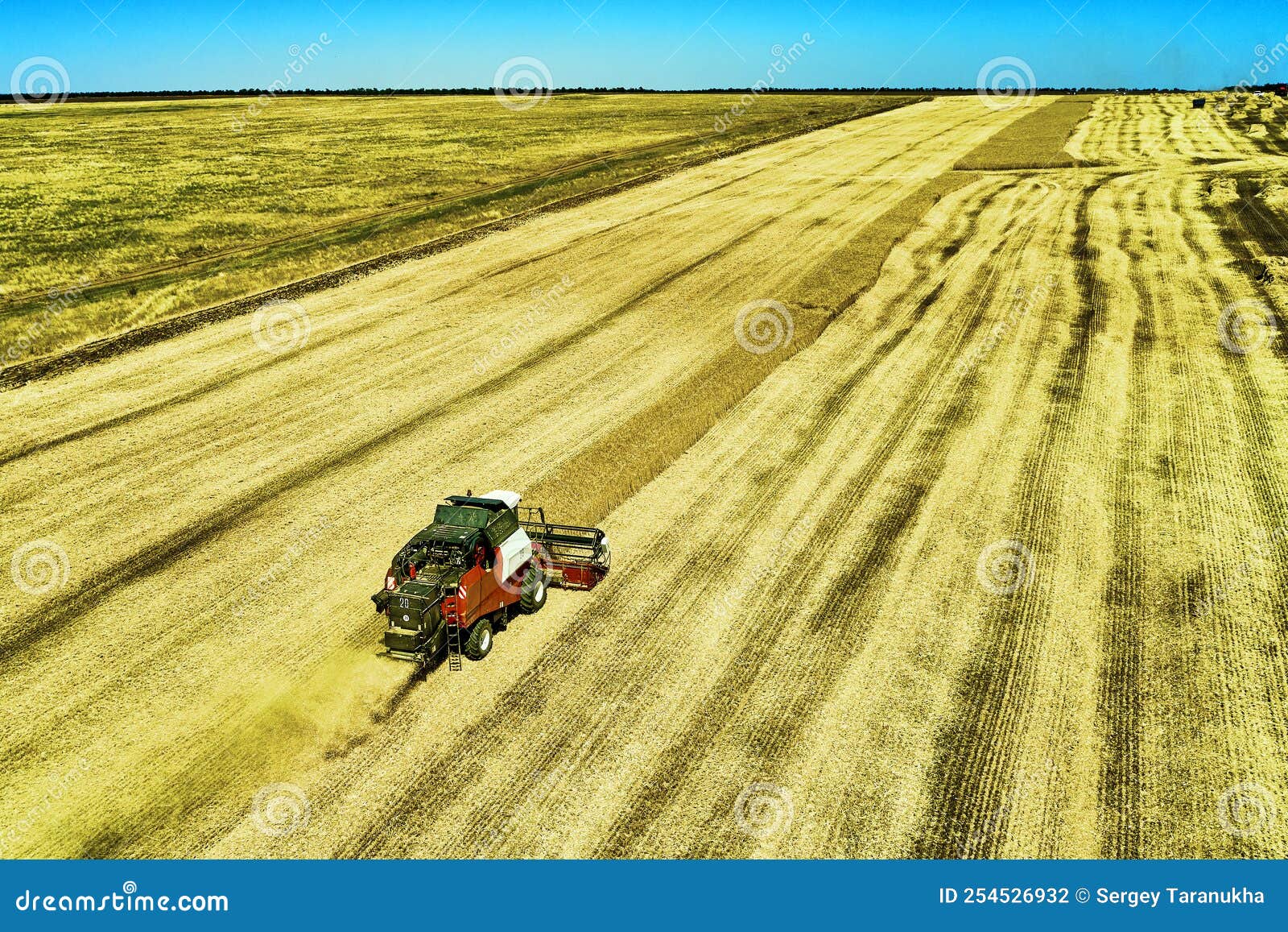 A Combine Harvester Harvesting a Field of Wheat Against a Blue Sky ... A Combine Harvester Harvesting a Field of Wheat Against a Blue Sky ...
