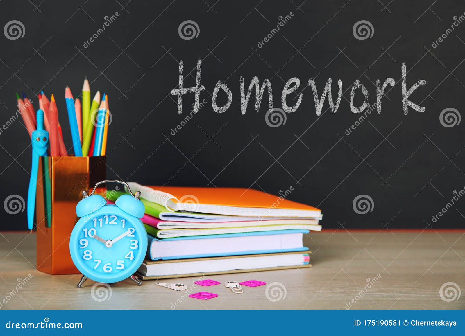 Composition with Stationery and Alarm Clock on Table Near Blackboard ...