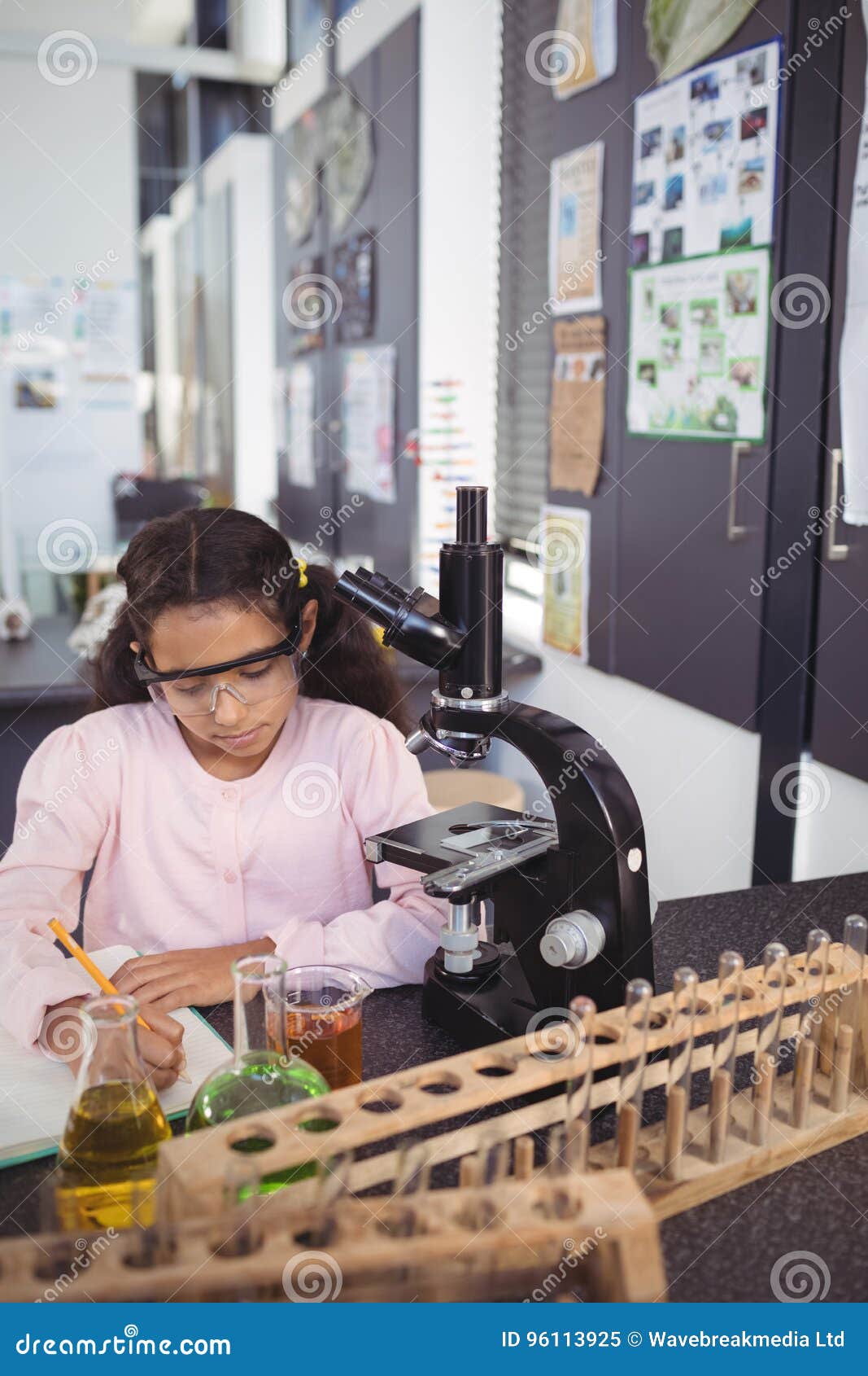 Concentrated Elementary Student Writing in Book by Microscope at ...