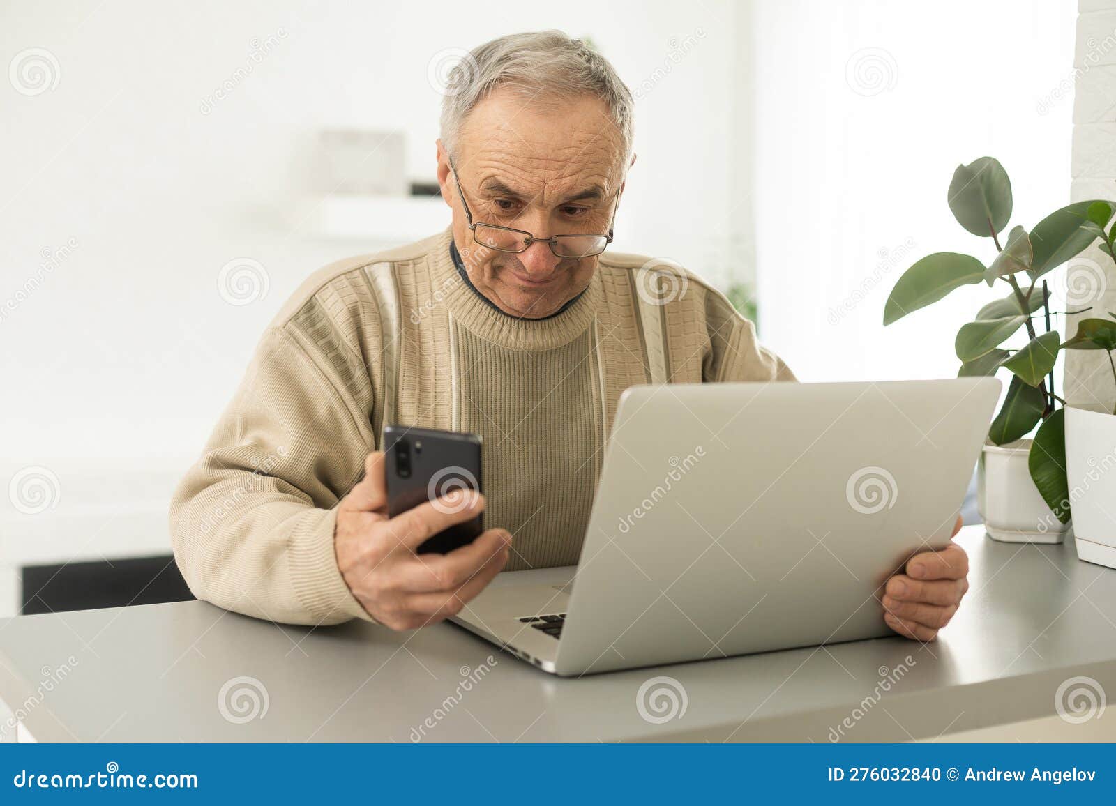 Concentrated Senior Man Looking at Laptop and Phone Calling at Home ...