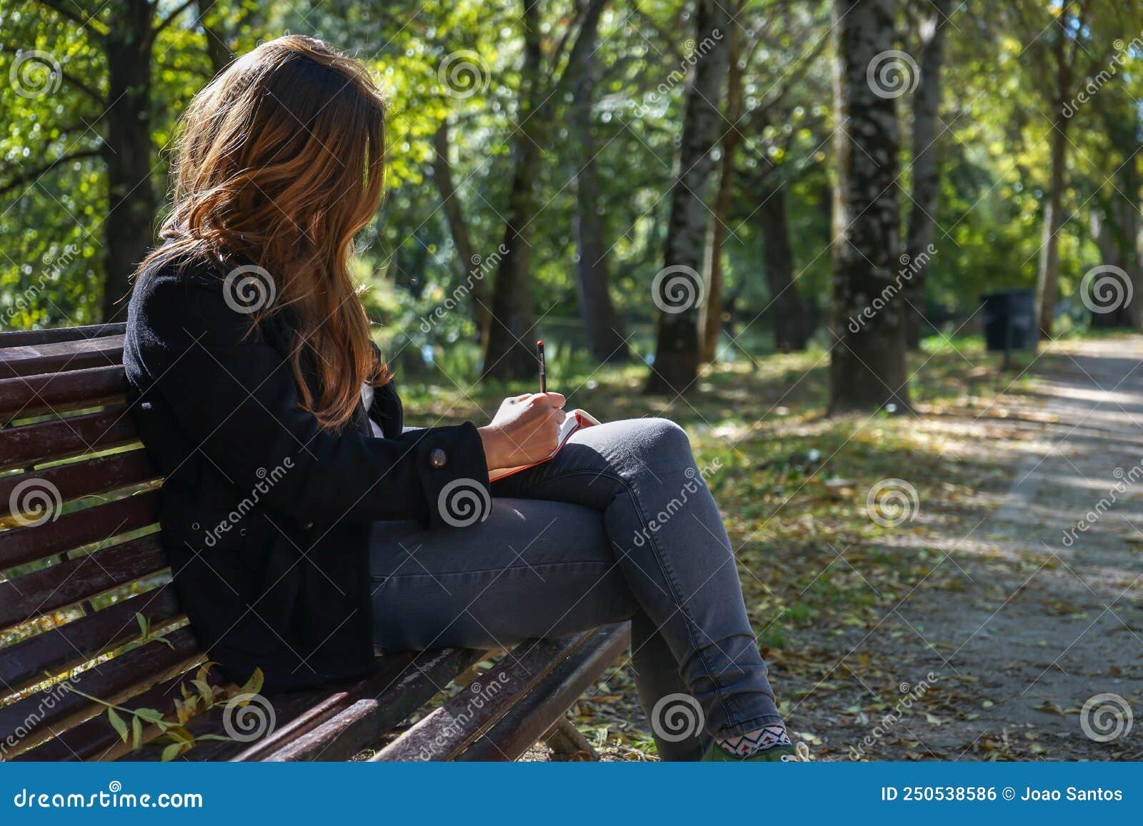 Concentrated Woman Writing on Notebook Sitting on a Bench in a Park ...