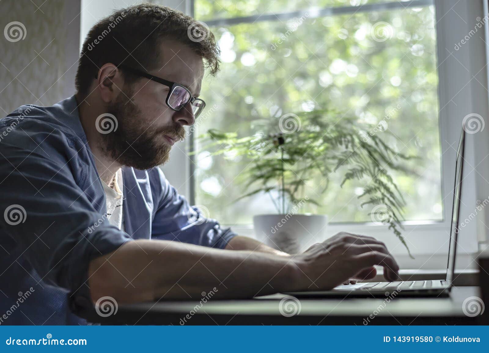 Concentrated Bearded Man In Glasses Works With A Laptop At Home