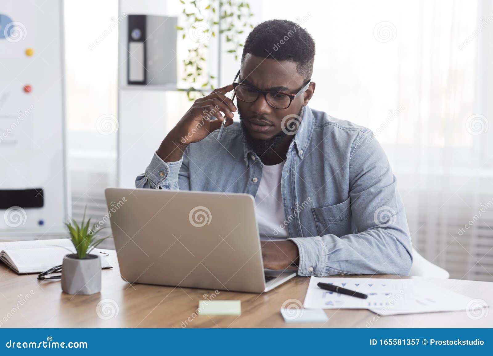 Concerned Black Employee Talking on Cellphone and Looking at Laptop ...