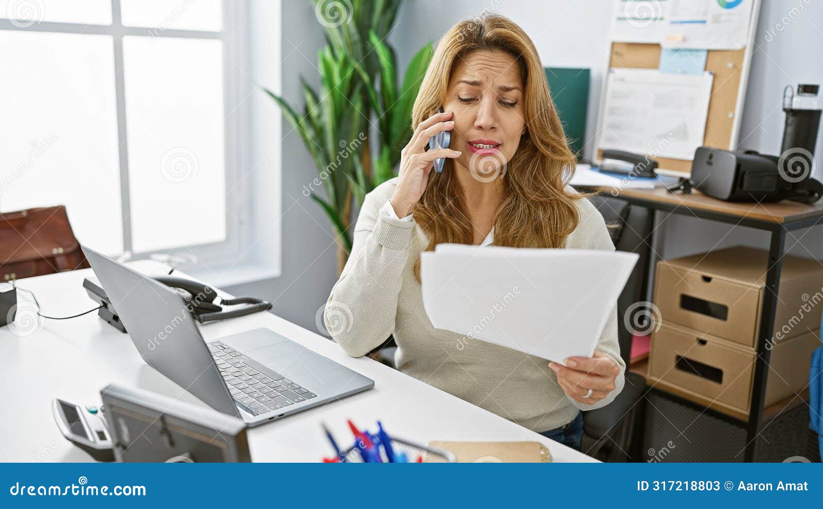 Concerned Hispanic Woman Multitasking in an Office Using Phone and ...