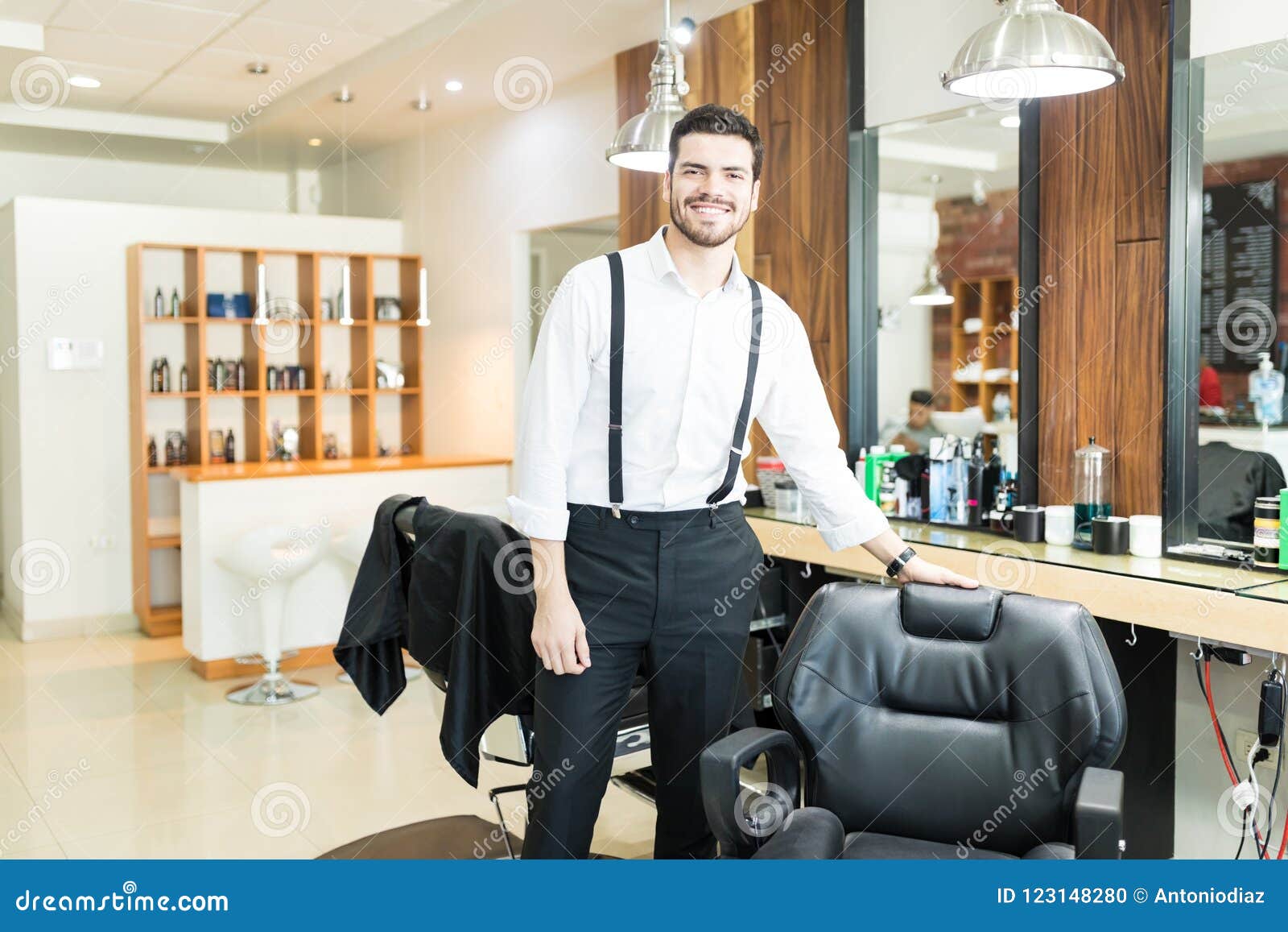 Confident Barber Smiling while Standing by Chair in Shop Stock Photo ... Confident Barber Smiling while Standing by Chair in Shop Stock Photo ...