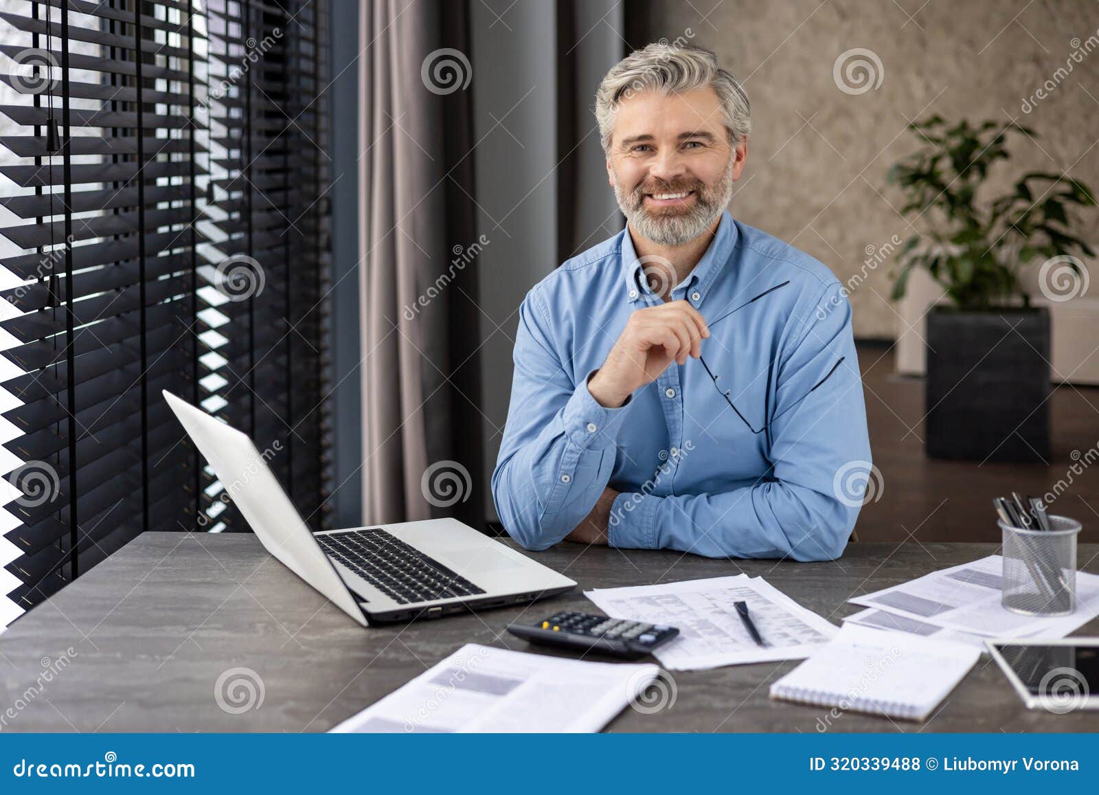 Smiling Businessman Working at Desk with Laptop and Documents in Modern ...