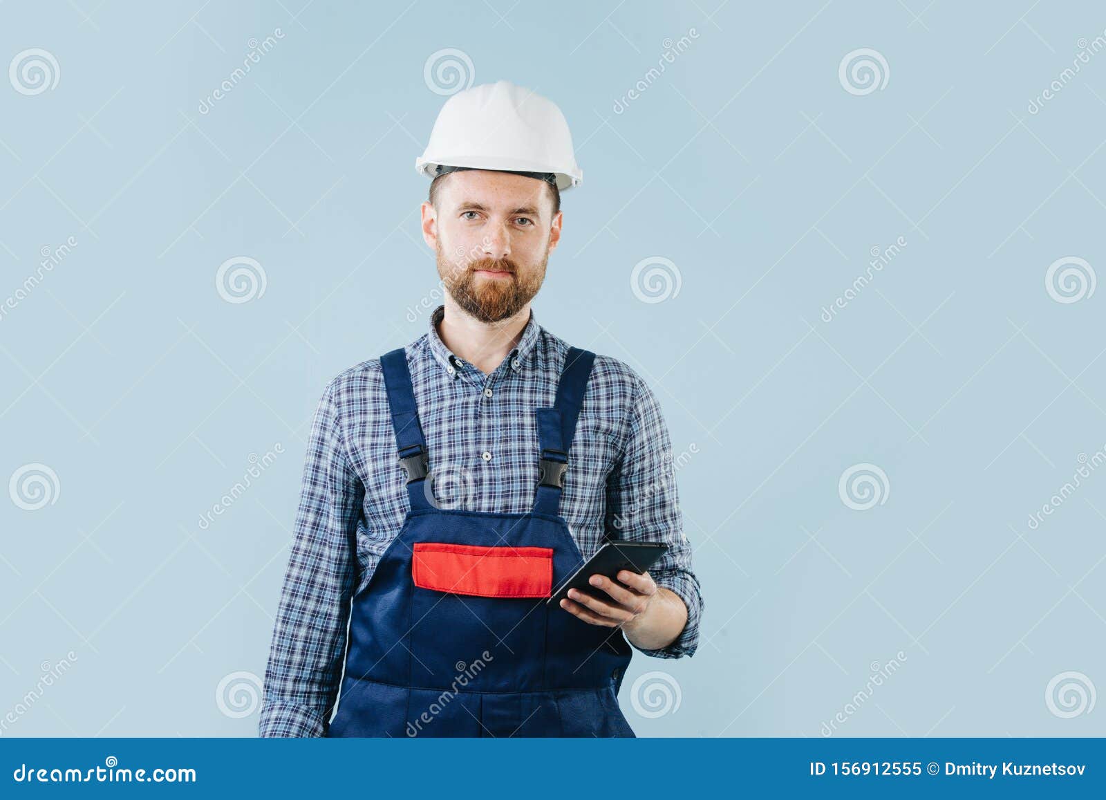 Confident Construction Worker in a White Helmet and Blue Overalls with ...