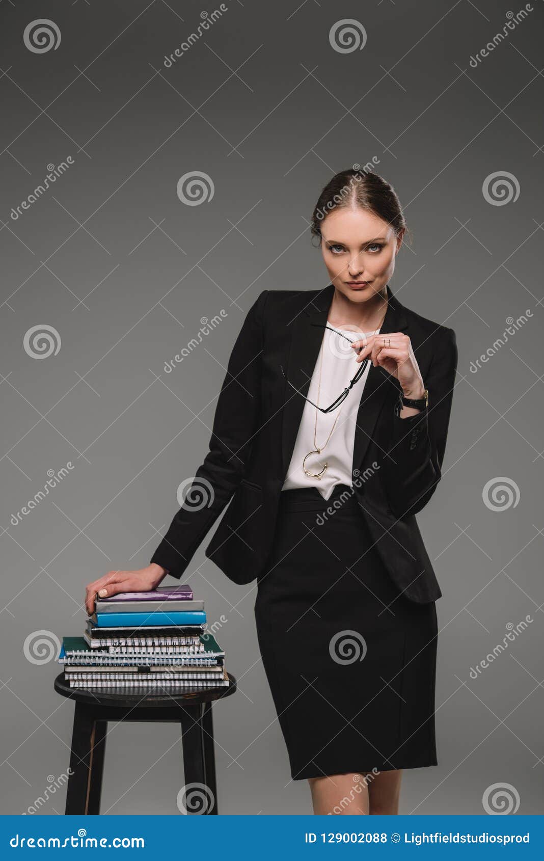 Confident Female Teacher Standing Near Chair with Stack of Textbooks on ... Confident Female Teacher Standing Near Chair with Stack of Textbooks on ...