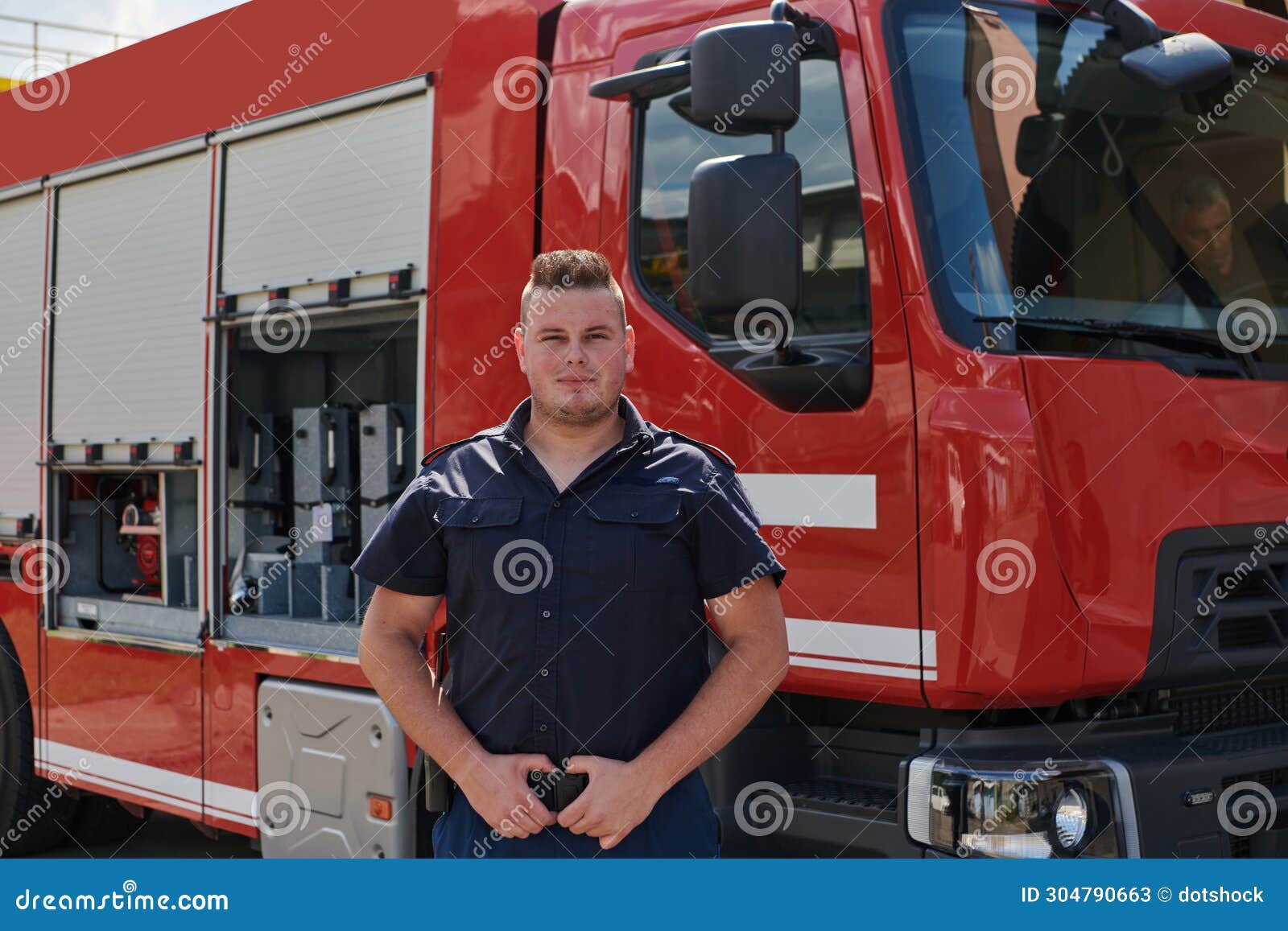 A Confident Firefighter Strikes a Pose in Front of a Modern Firetruck ...