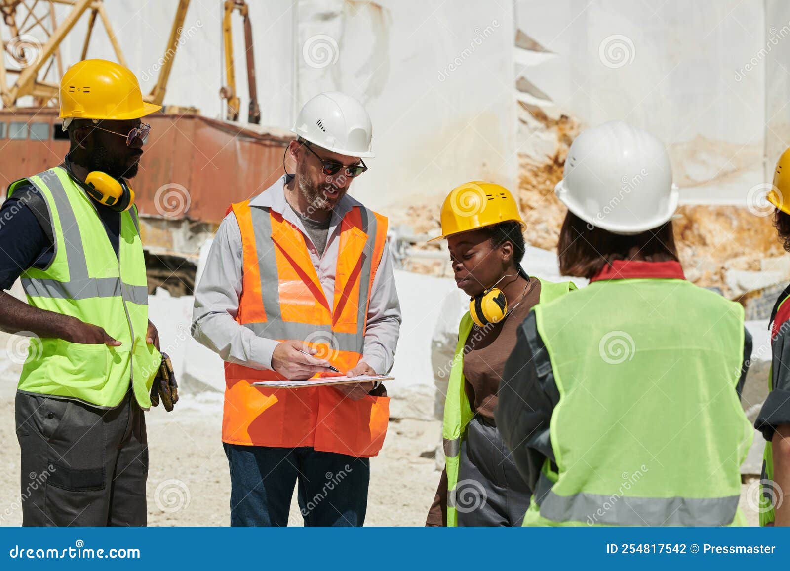Confident Foreman in Uniform and Safety Helmet Pointing at Document ...