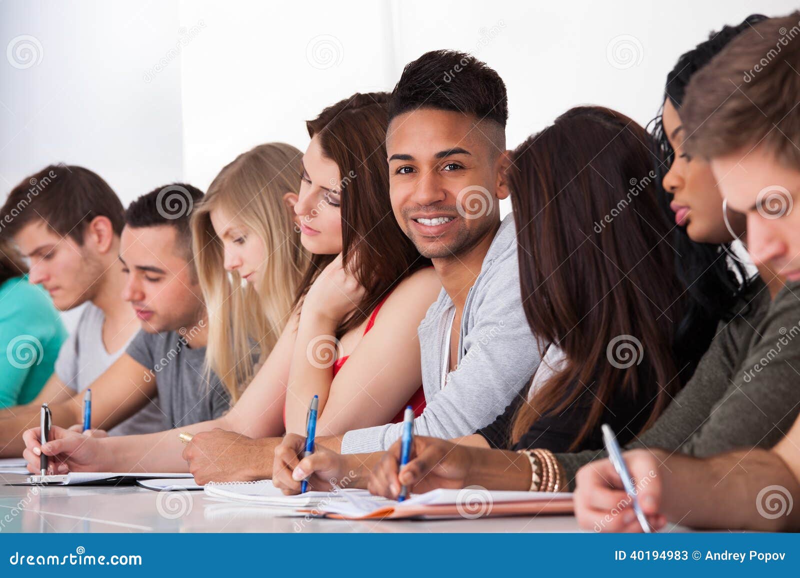 Confident Student Sitting with Classmates Writing at Desk Stock Image ...
