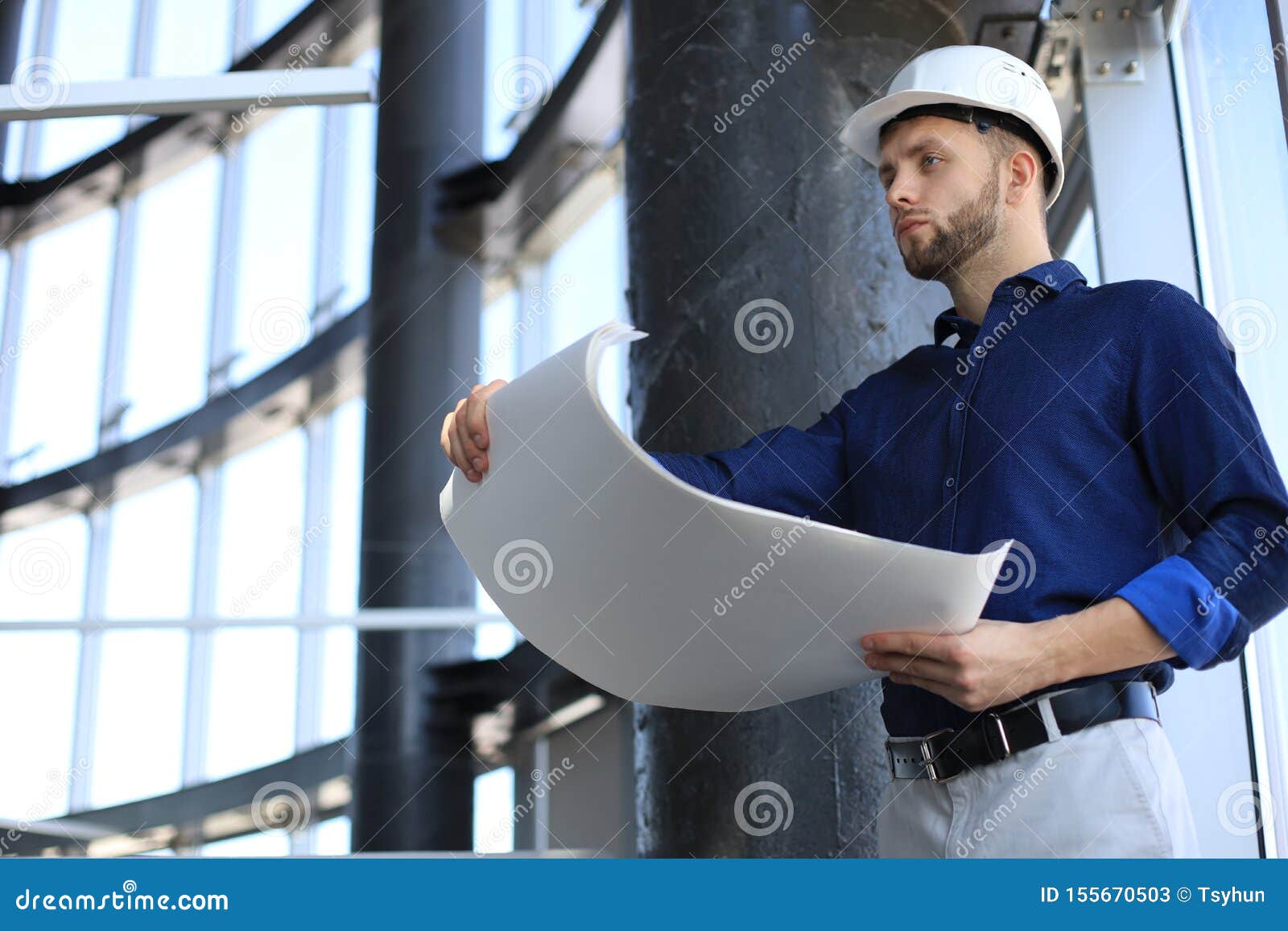 Confident Young Architect in Navy Shirt and Hardhat Holding a Blueprint ... Confident Young Architect in Navy Shirt and Hardhat Holding a Blueprint ...