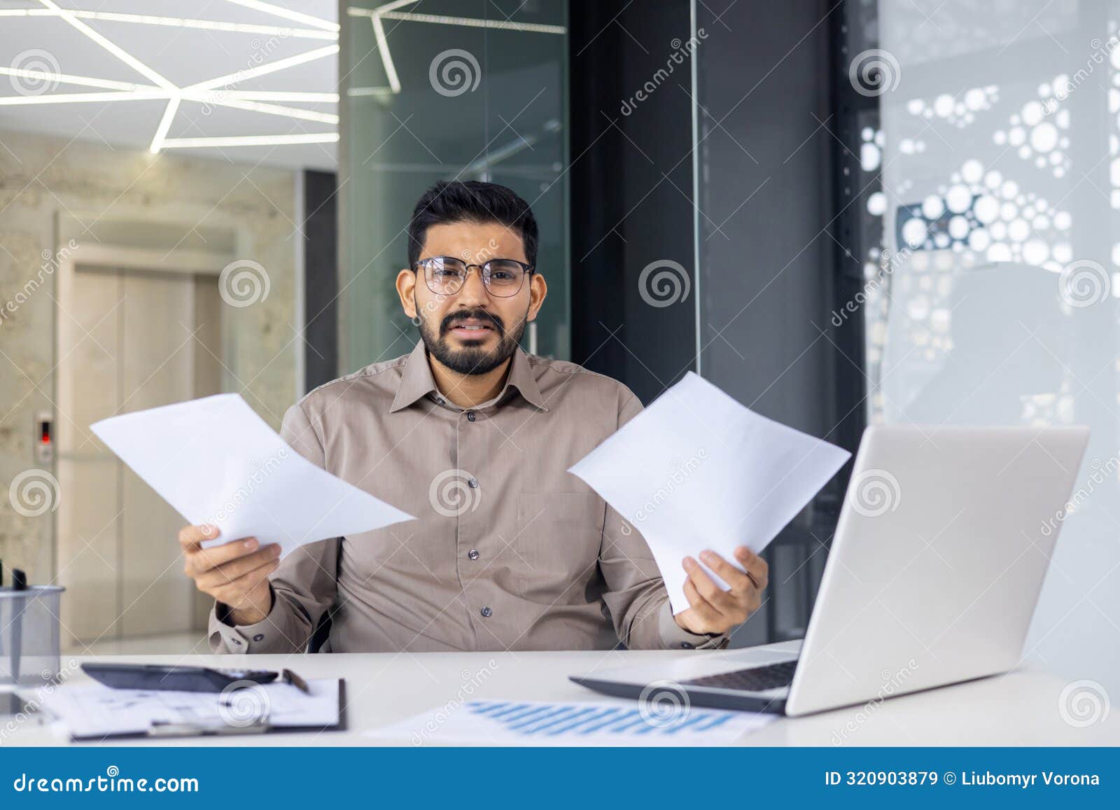 Confused Businessman Holding Documents while Working at Laptop in ...