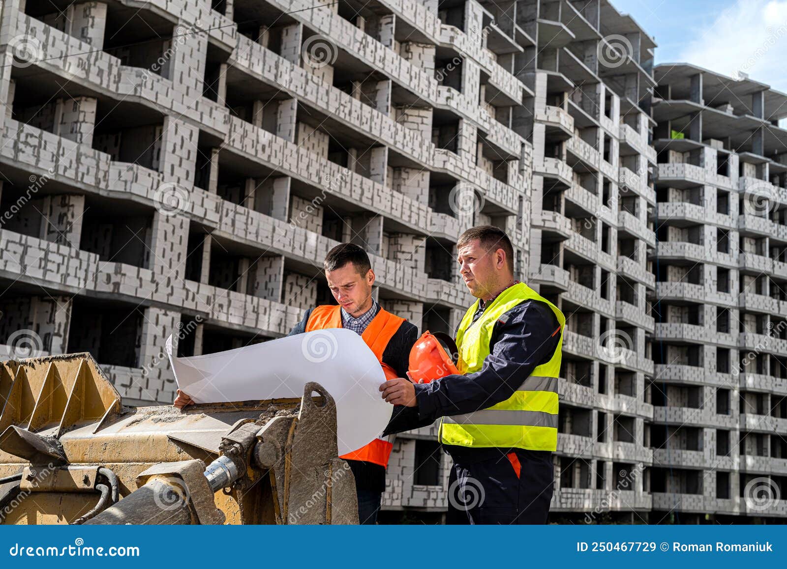 On a Construction Site, One Worker in Uniform Shows Another Worker in ...