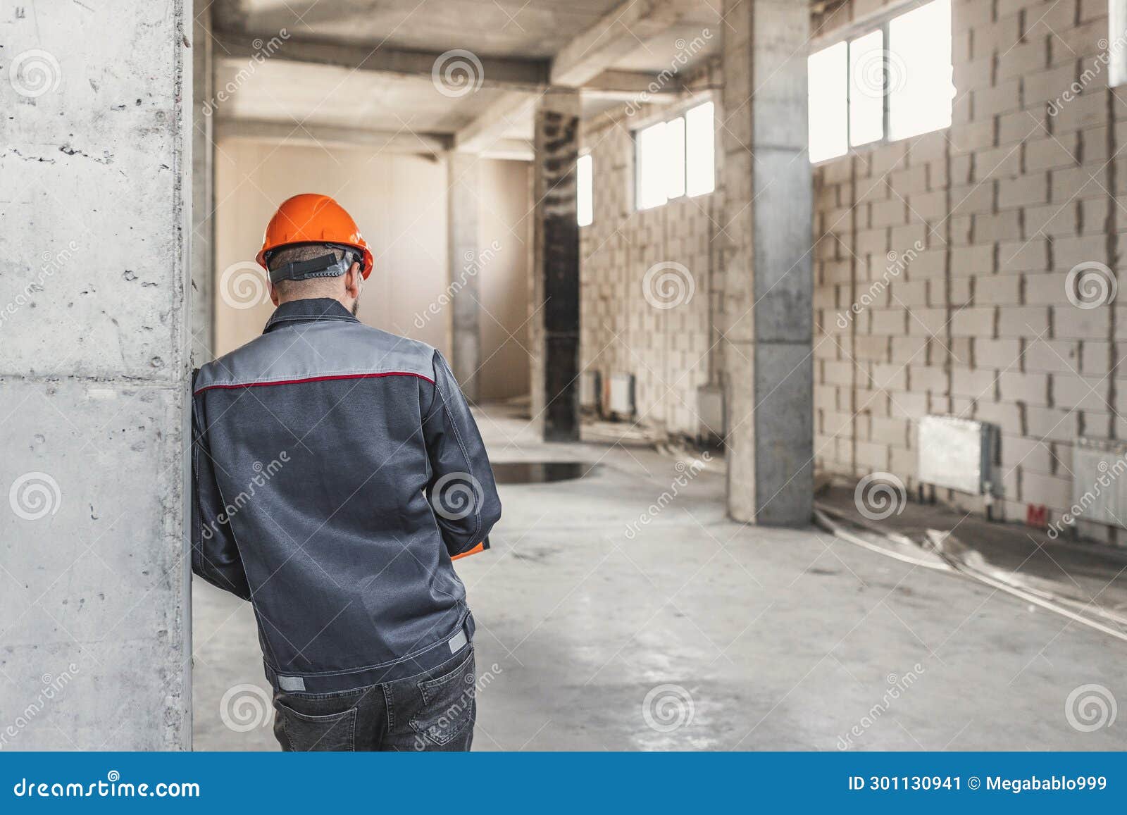 A Construction Worker in a Helmet Stands with His Back To the Camera ...