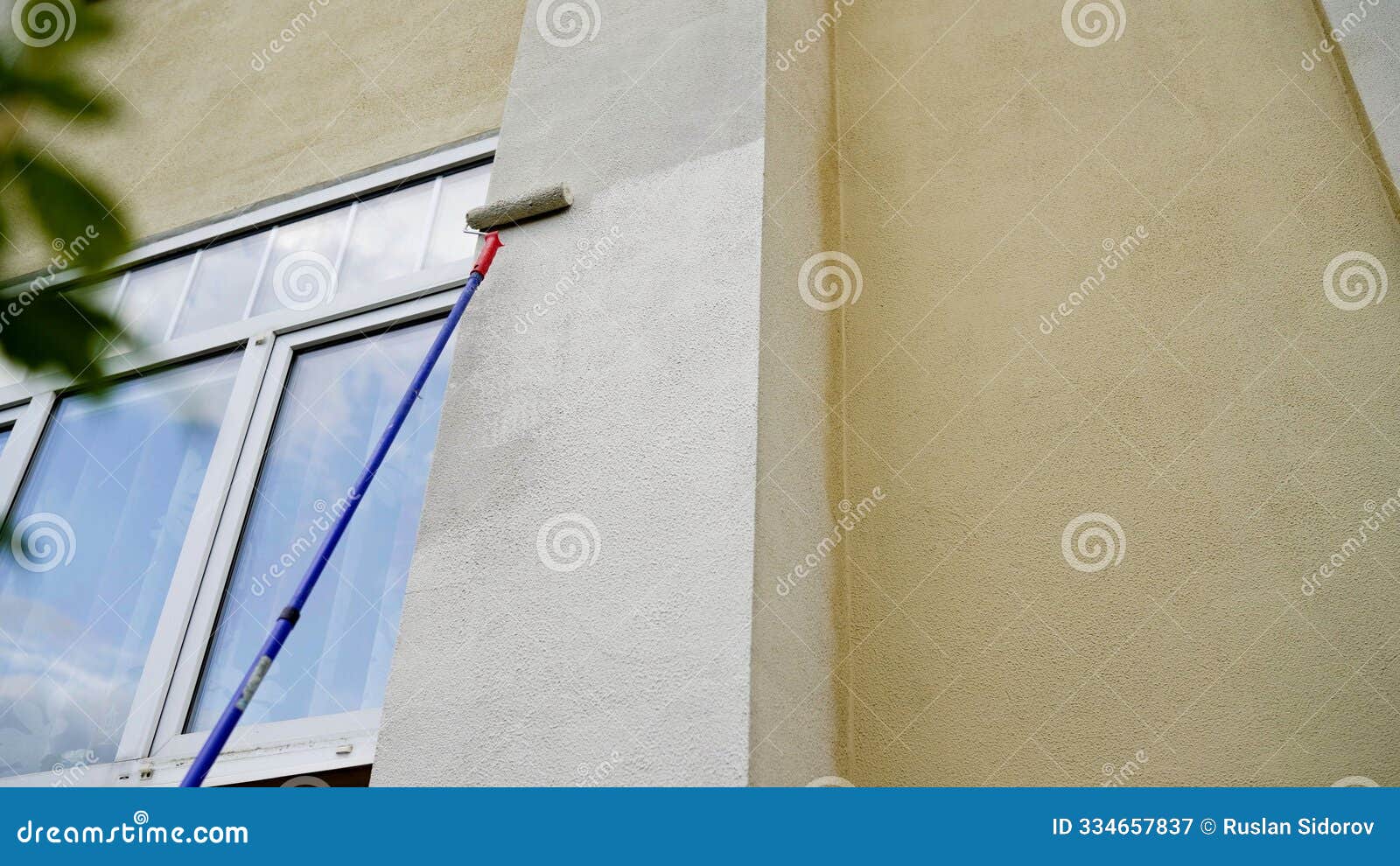 Construction Worker is Painting a Building Using a Paint Roller on a ...