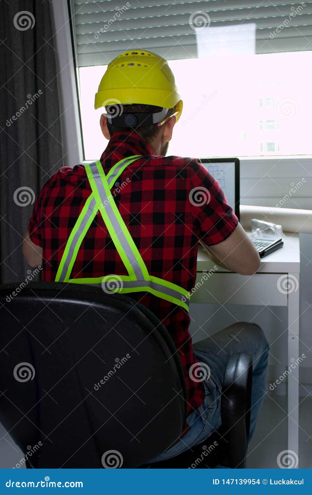 Construction Worker is Sitting at His Desk at the Computer, Looking at ...