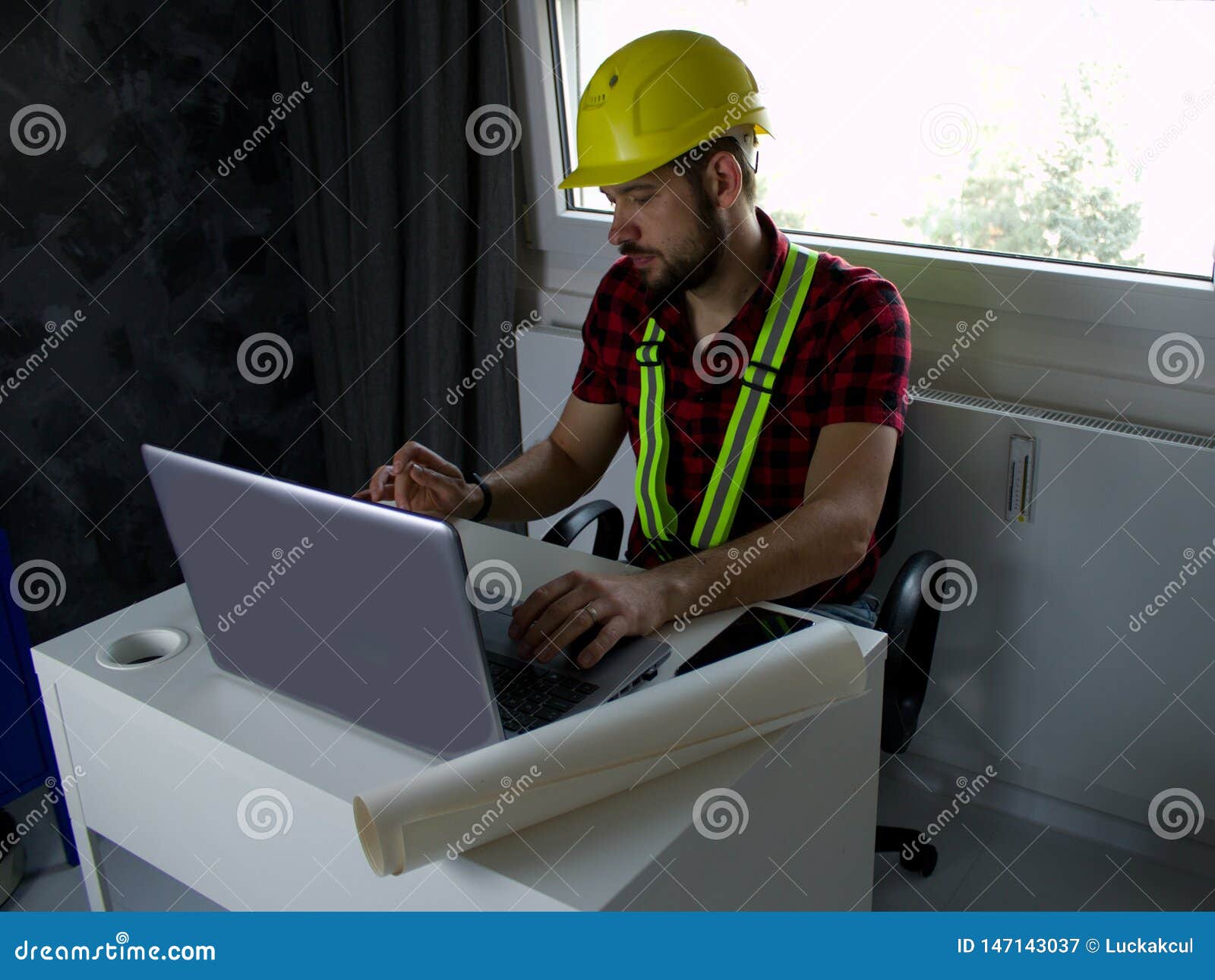 Construction Worker is Sitting at His Desk at the Computer, Looking at ...