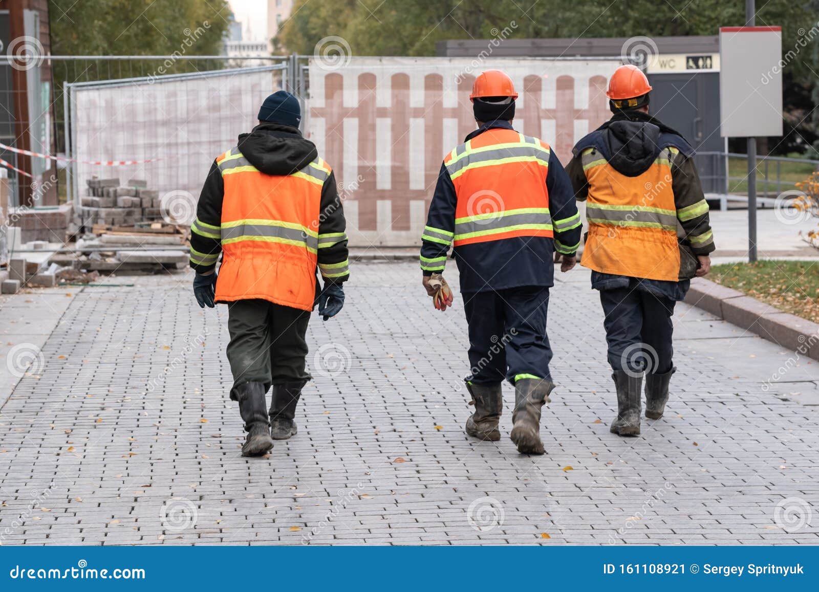 Construction Workers in Orange Vests Walking Along the Road in the ...
