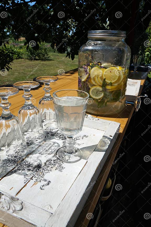 A Container with Lemonade and Glasses on a Table in the Yard of the ...