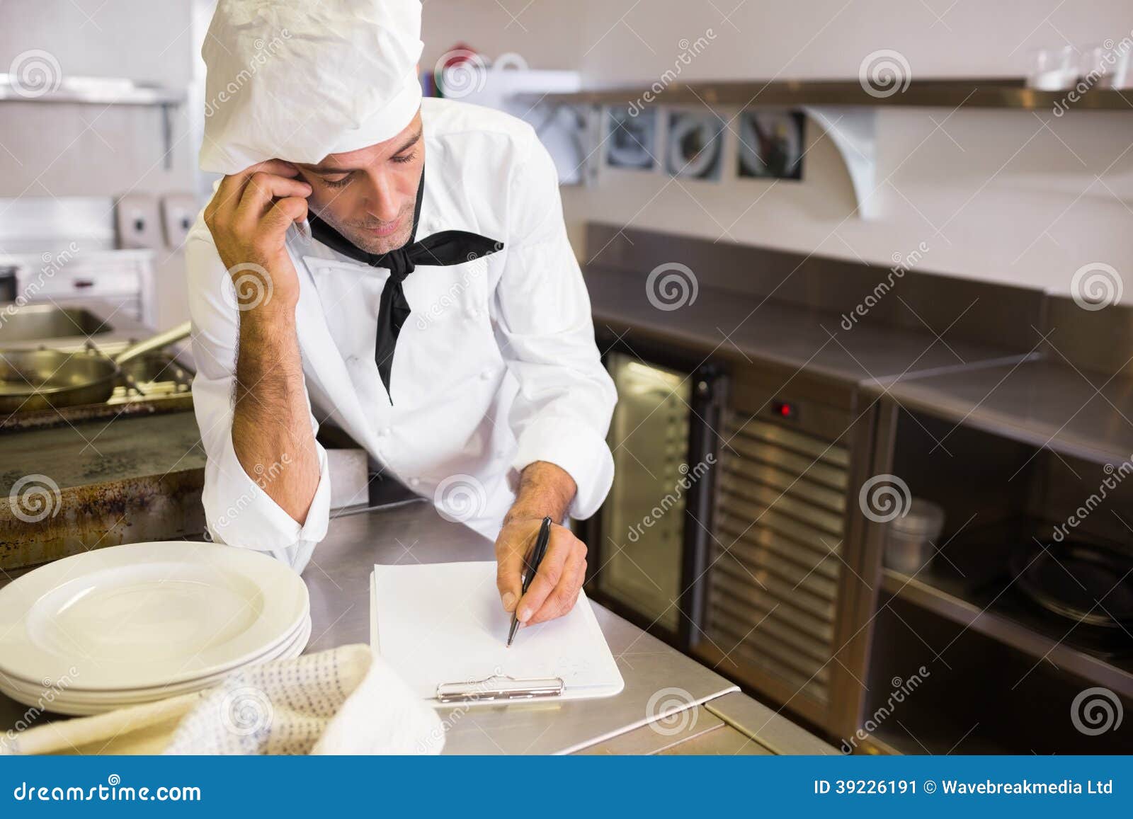 Cook Writing on Clipboard while Using Cellphone in Kitchen Stock Image ...