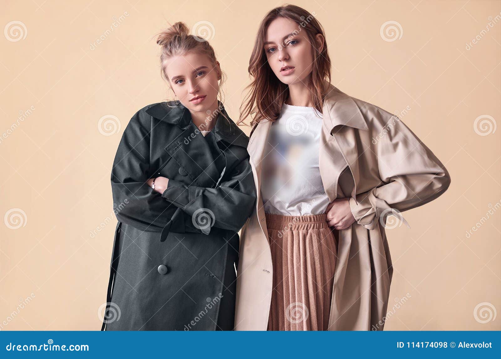Coppia Le Belle Ragazze Dei Pantaloni A Vita Bassa Che Portano I Cappotti Lunghi Di Modo Sulla