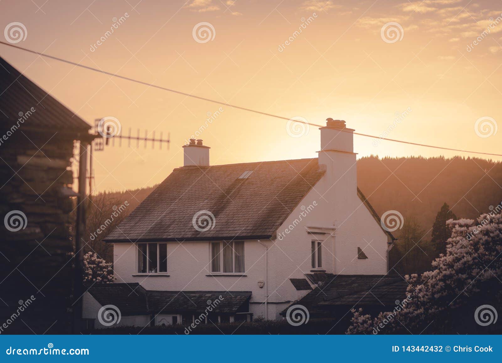 A Cosy Thatched English Cottage with the Warm Orange Sun Setting Behind ...