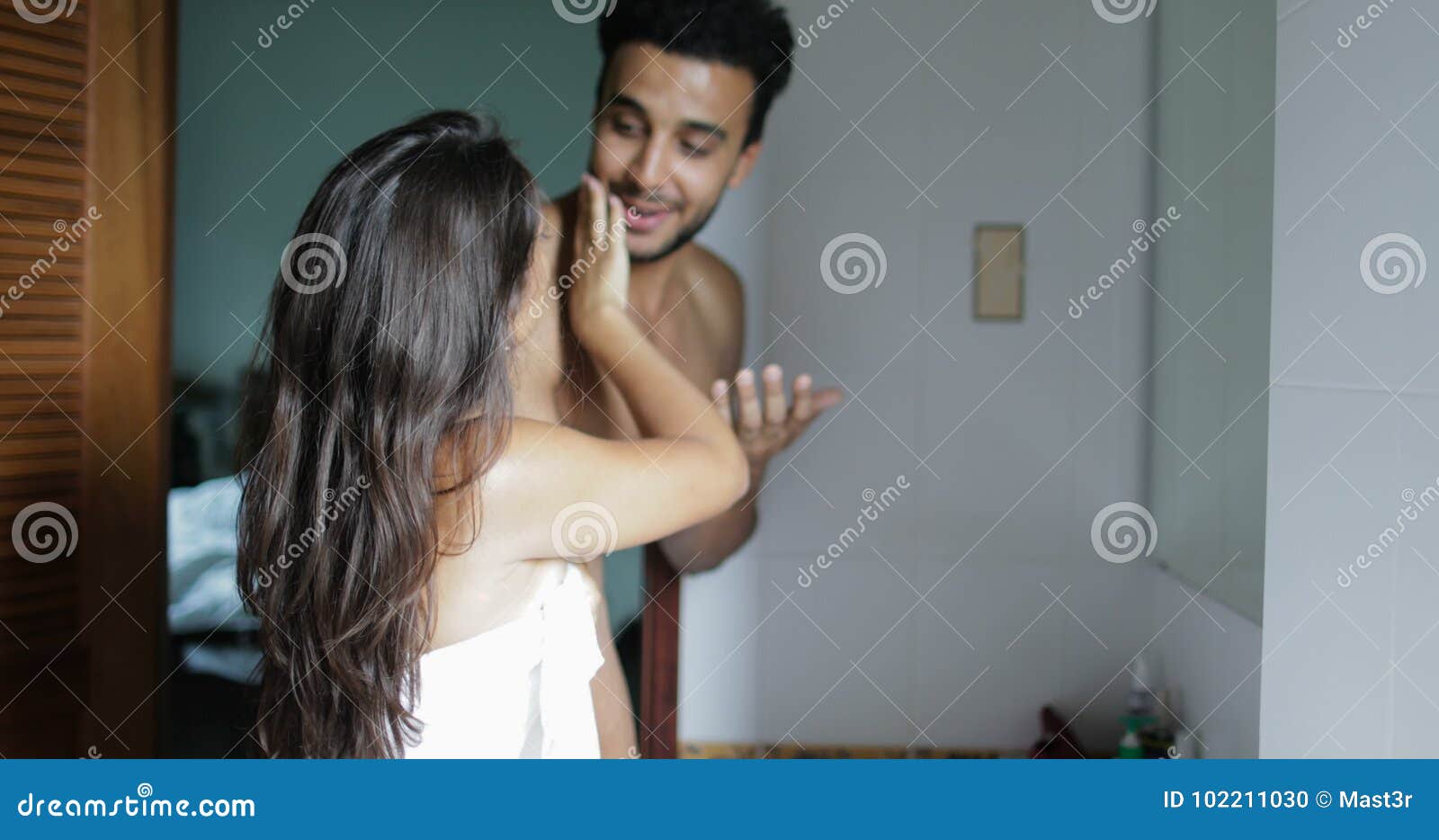 Couple In Bathroom Woman Washing Face Talking To Man In Towels Doing