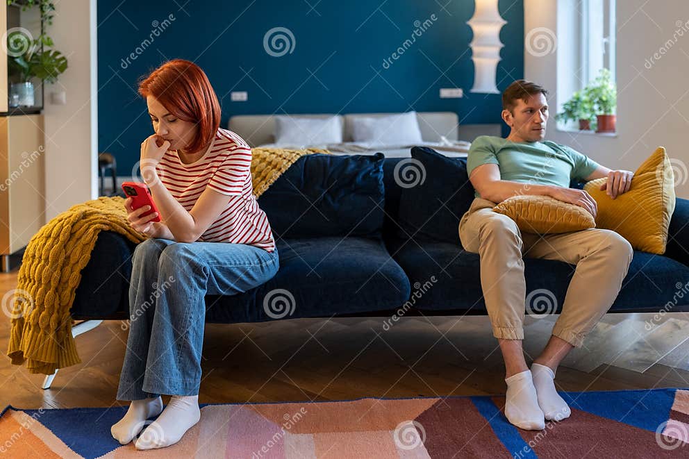 Couple Man And Woman Ignoring Each Other Wife In Phone Husband Sitting Near On Couch Stock
