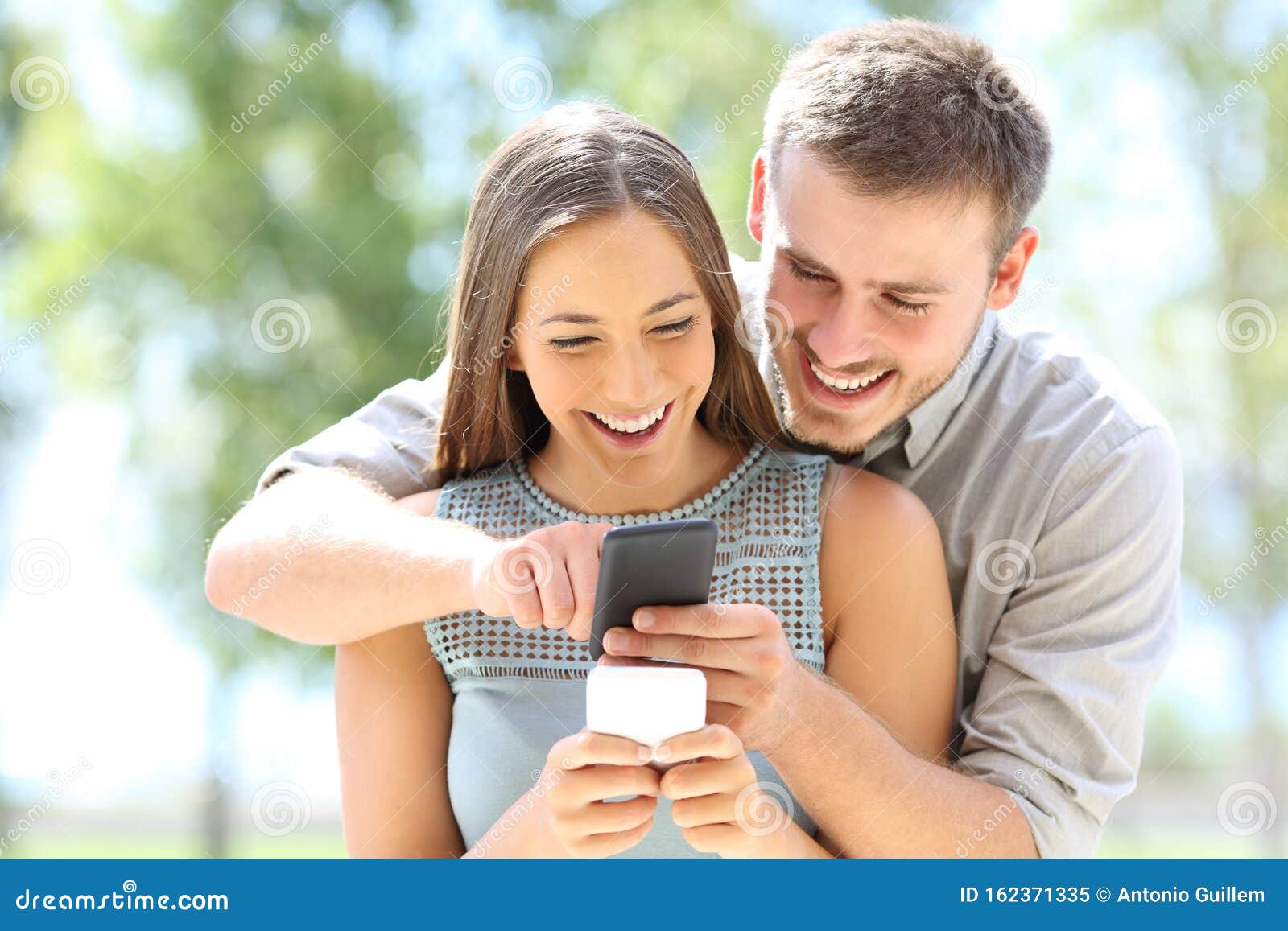 Couple Sharing Smart Phone Content in a Park Stock Image - Image of ...