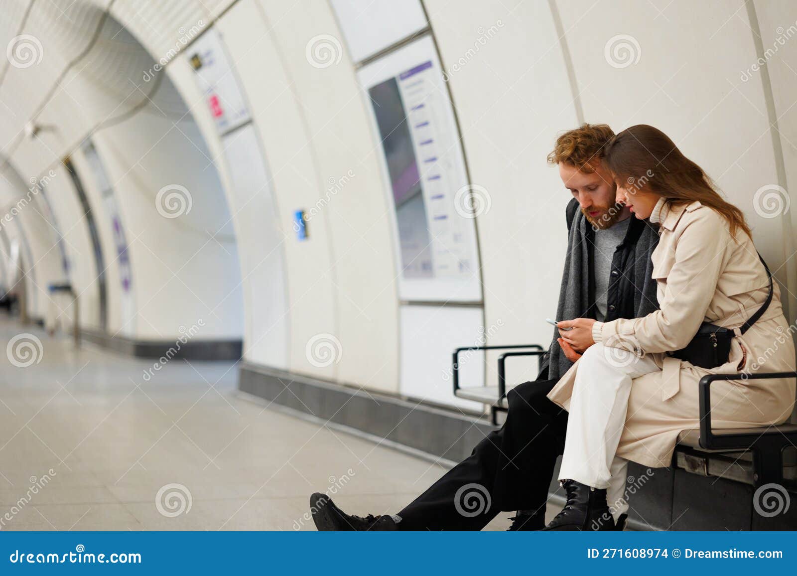 Couple is Sitting on a Subway Station Bench and Watching Something on a ...