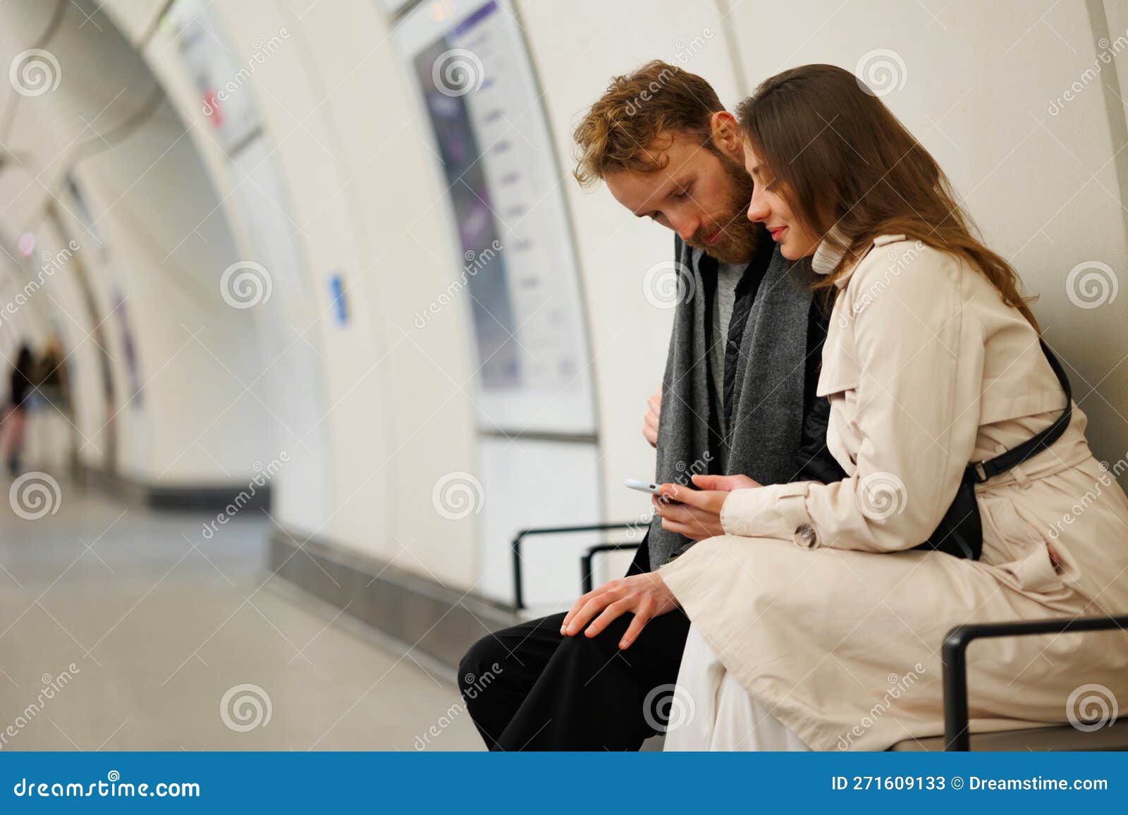 Couple is Sitting on a Subway Station Bench and Watching Something on a ...