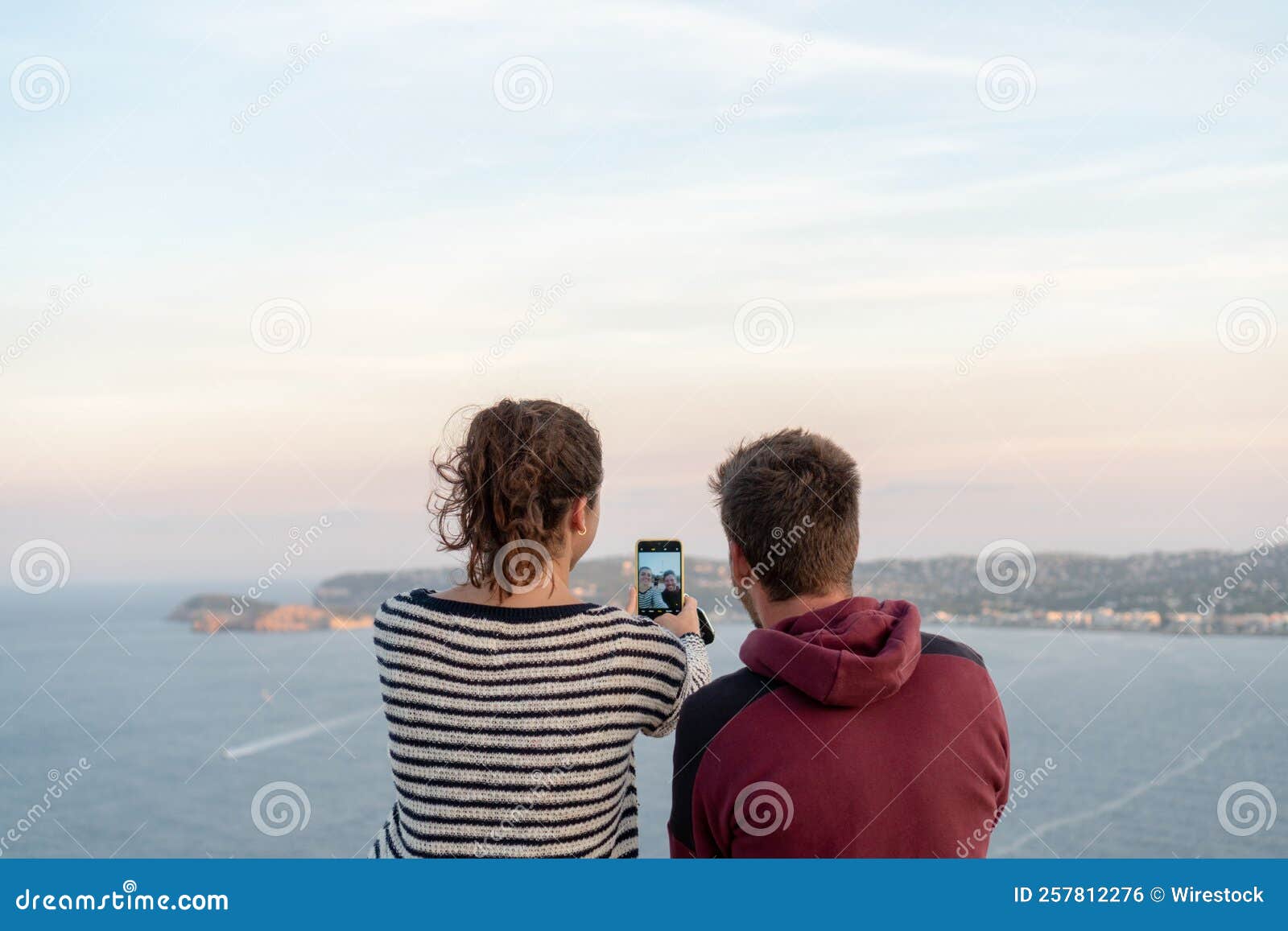 Couple Sitting And Taking Selfies With The Beautiful Seascape At Sunset